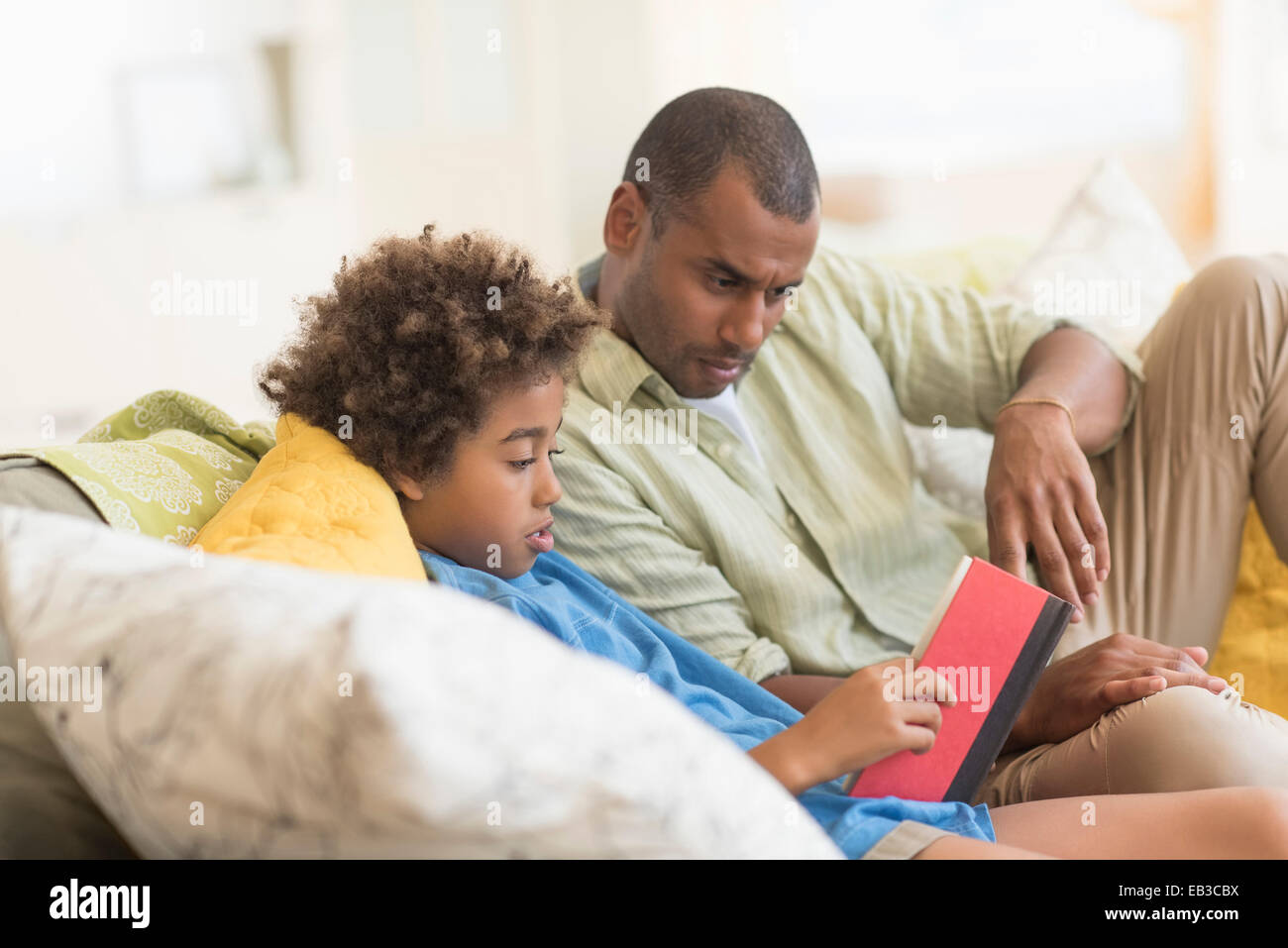 Father and son reading book in living room Stock Photo - Alamy