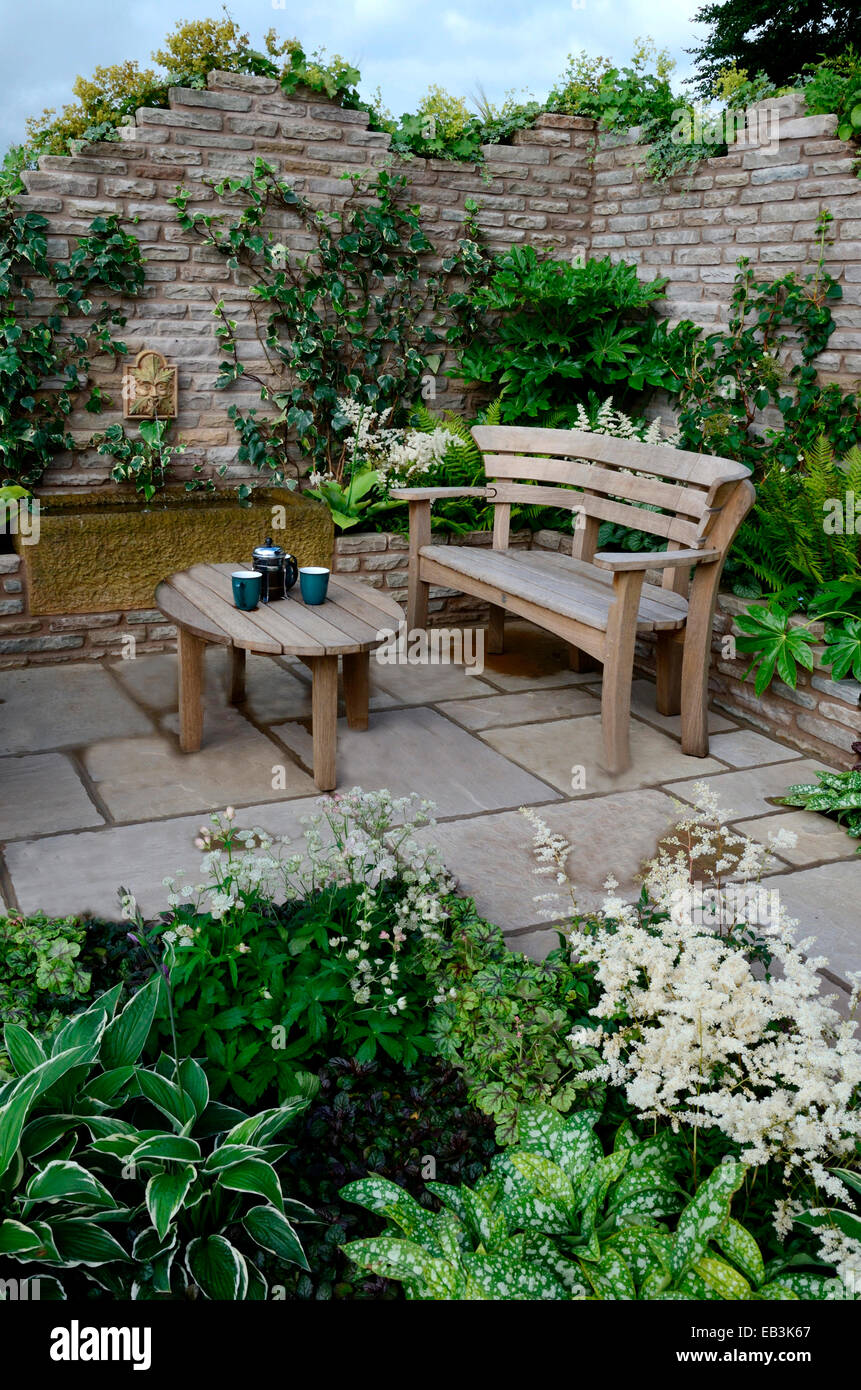 Close up of a wooden garden seat and table in a walled garden patio ...