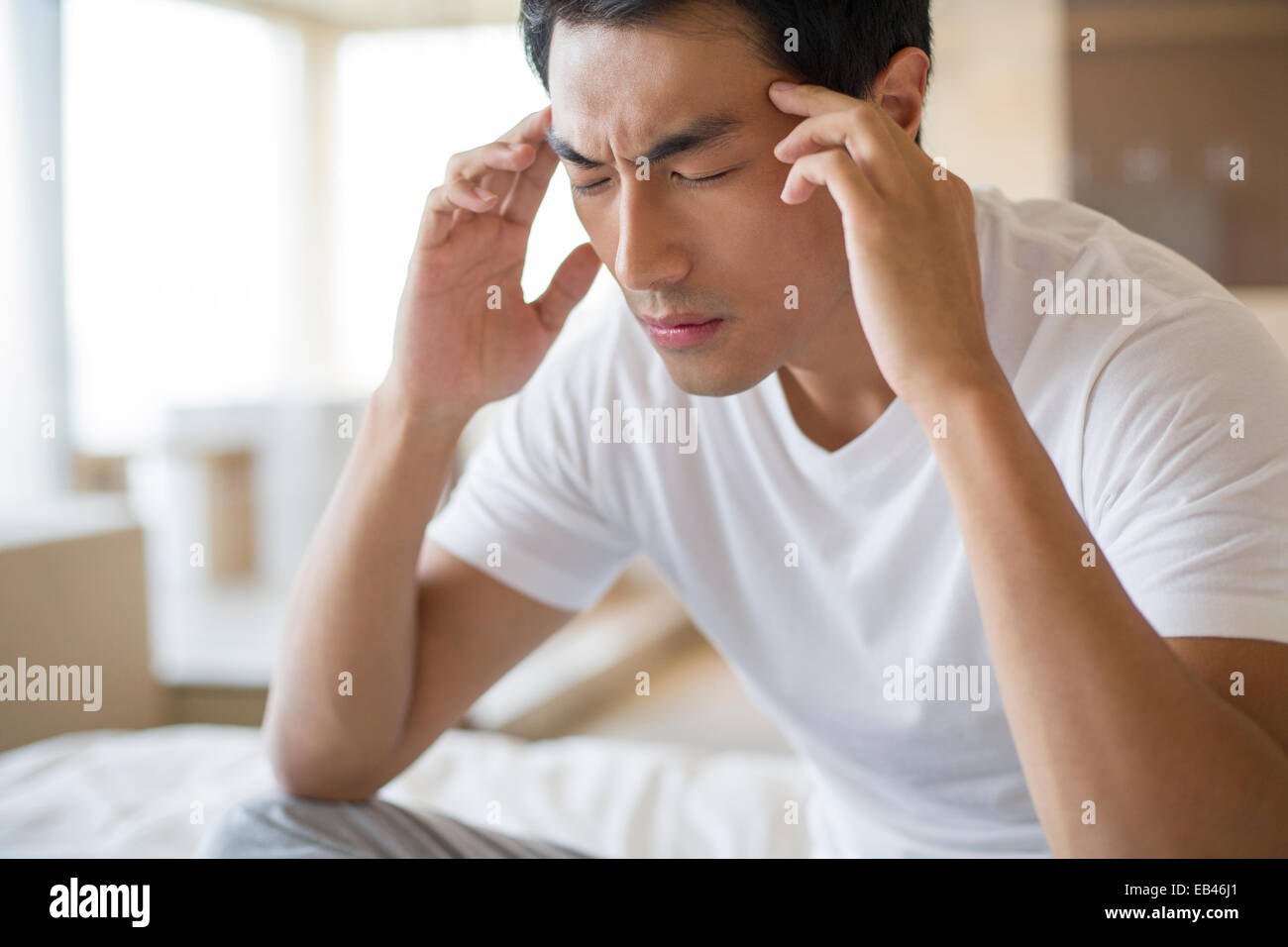 Young man rubbing temples on bed Stock Photo - Alamy
