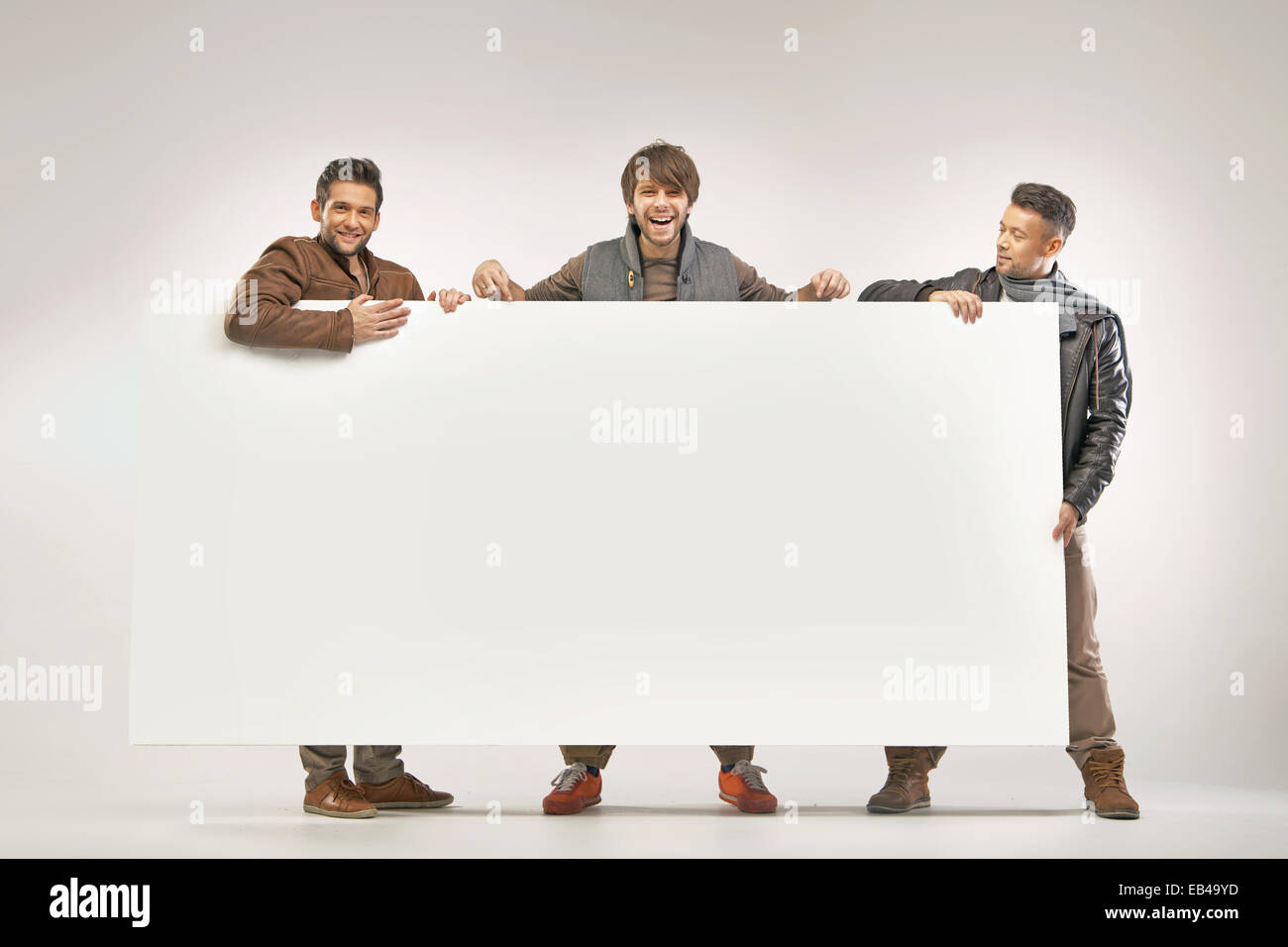 Three cheerful guys holding the empty board Stock Photo - Alamy