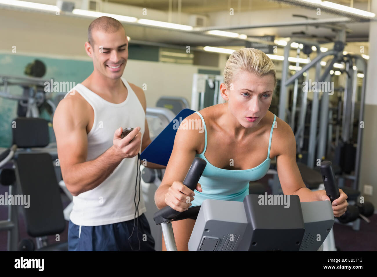 Trainer timing his client on exercise bike at gym Stock Photo - Alamy