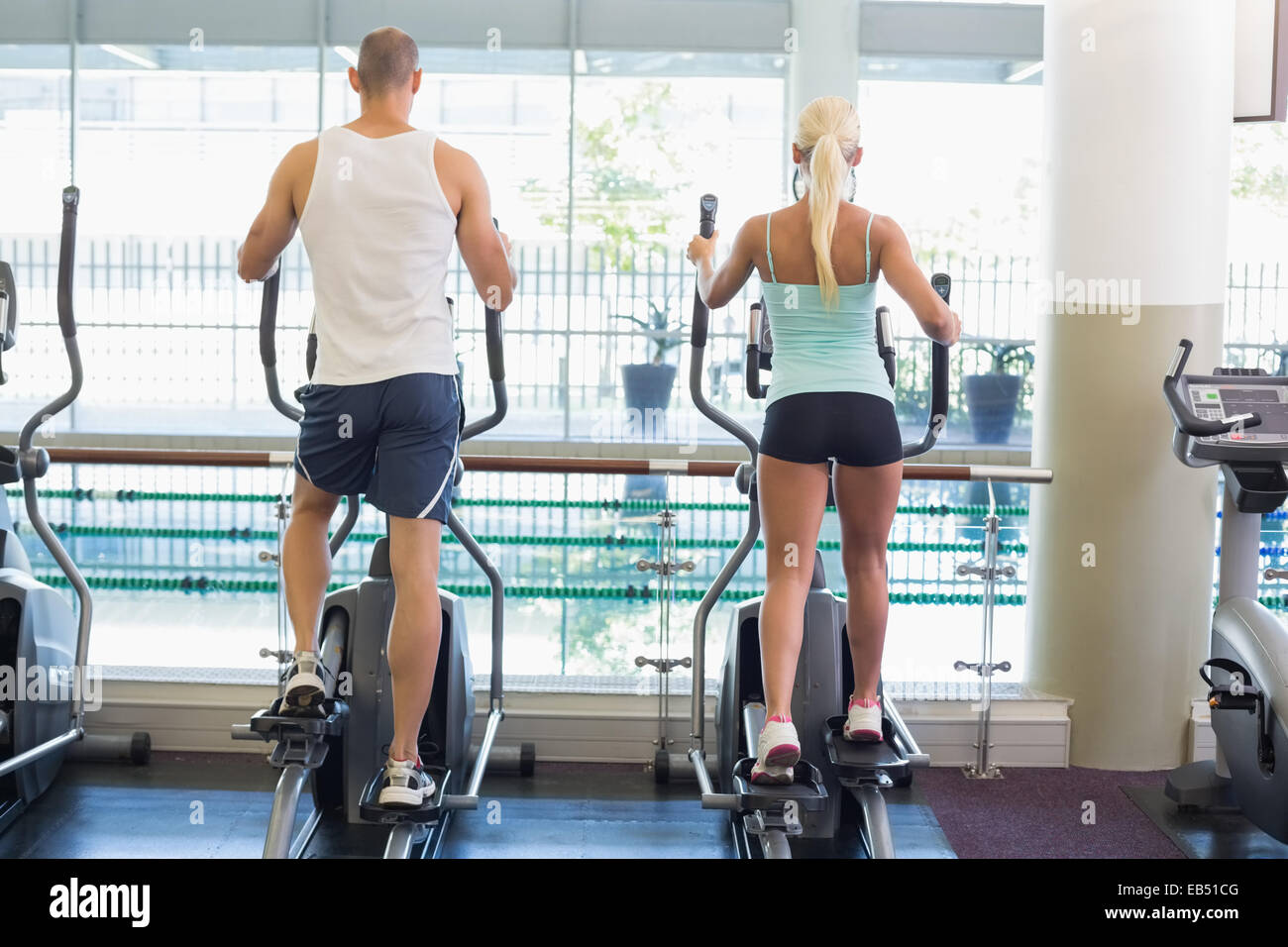 Rear view of couple working on x-trainers at gym Stock Photo - Alamy