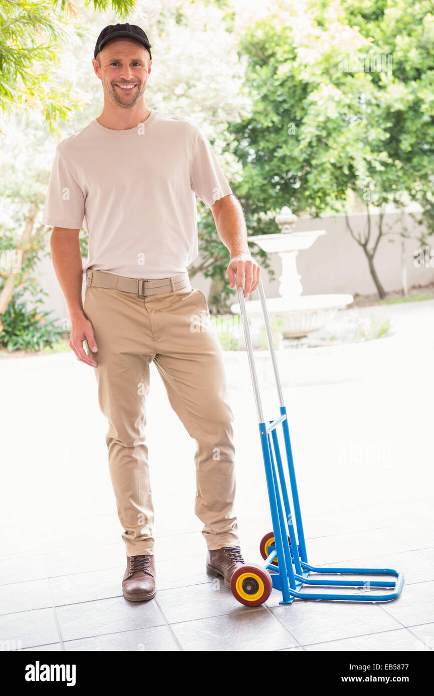 Happy delivery man leaning on trolley Stock Photo - Alamy
