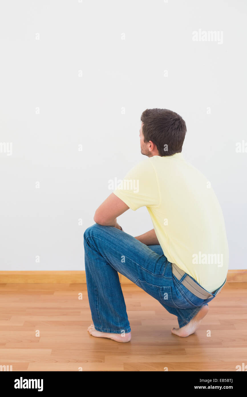 Casual man crouching on floor looking at wall at home Stock Photo - Alamy