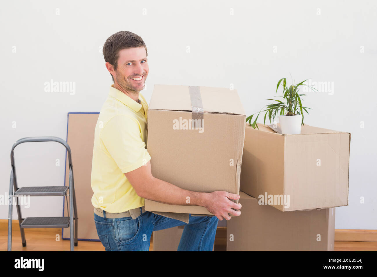 Smiling man carrying cardboard moving boxes at home Stock Photo - Alamy