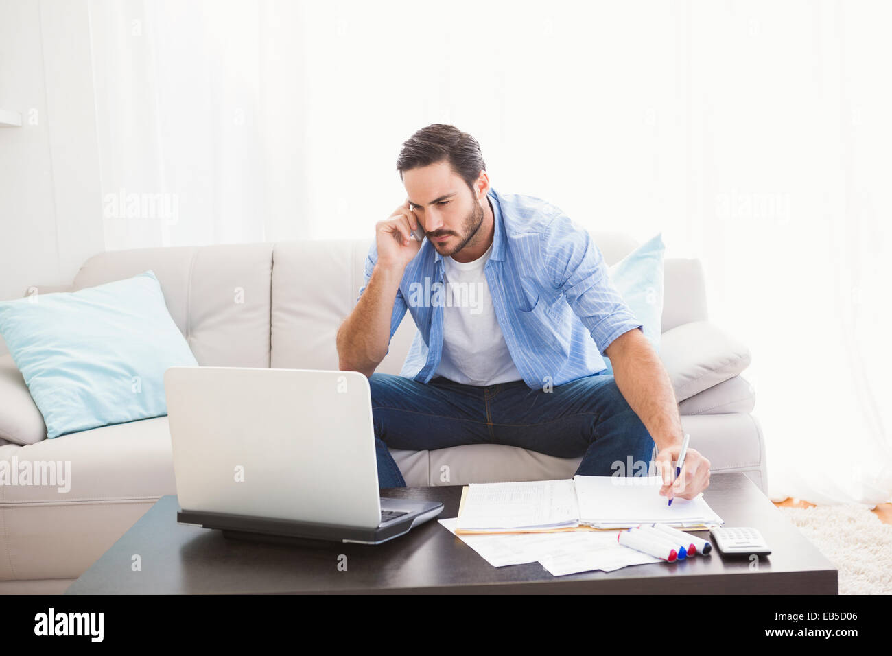 Man paying his bills with laptop while talking on phone Stock Photo - Alamy