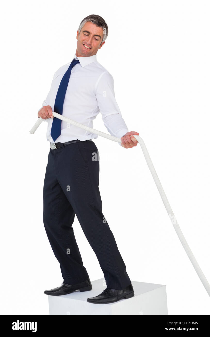 Smiling businessman standing on a cube and pulling rope Stock Photo - Alamy
