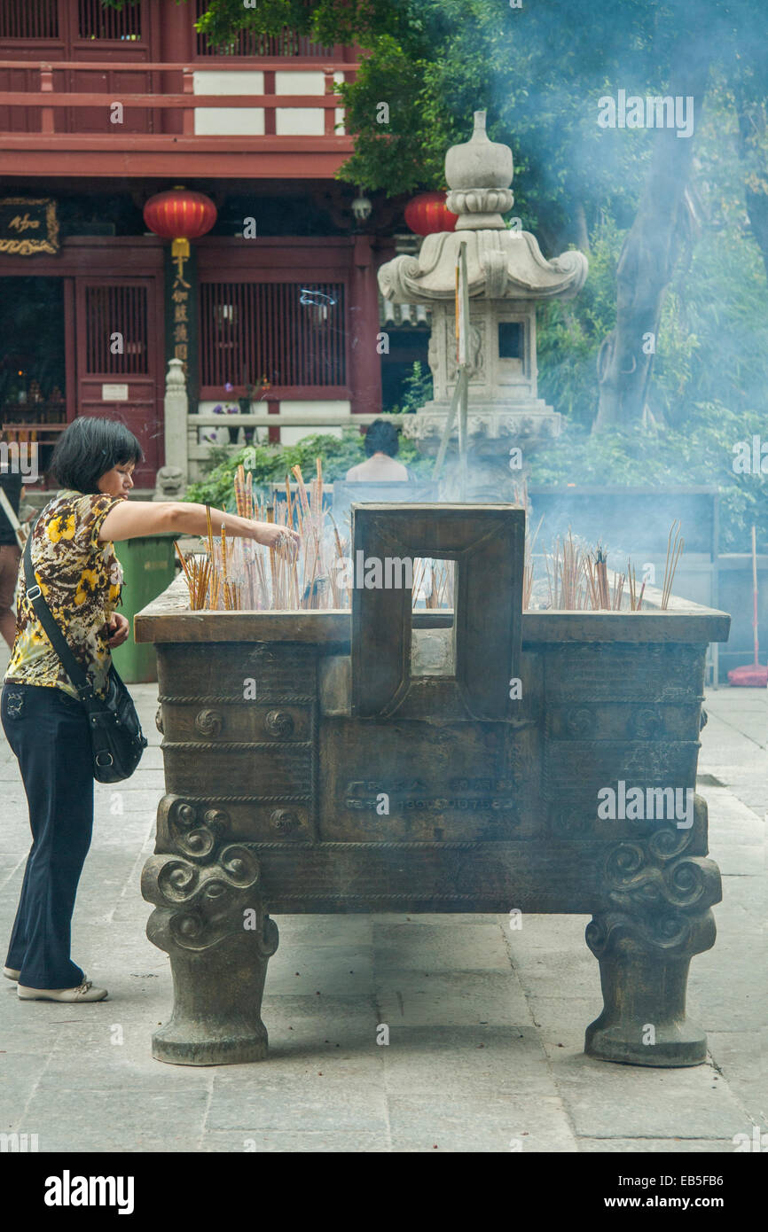 one woman placing pray sticks into ornamental earn at a Chinese shrine ...