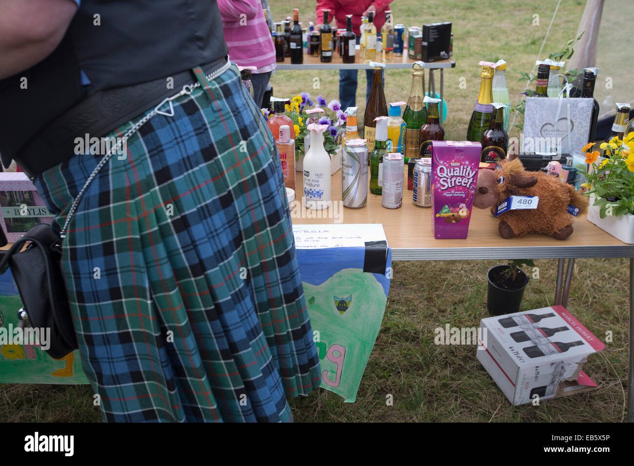 A man in a Scottish kilt walking past a stall with raffle prizes at the ...