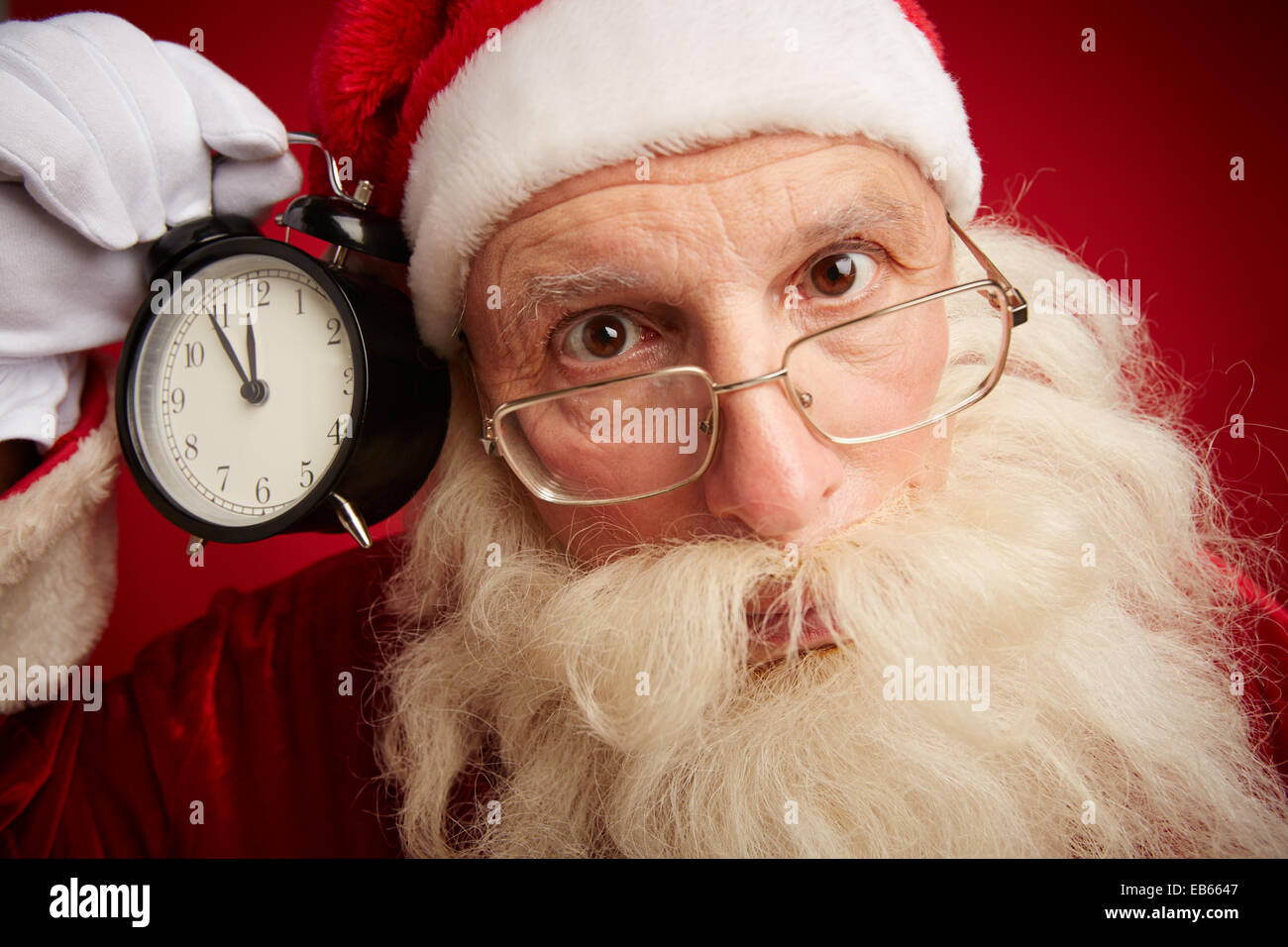 Puzzled Santa holding clock showing five minutes to xmas and looking at ...