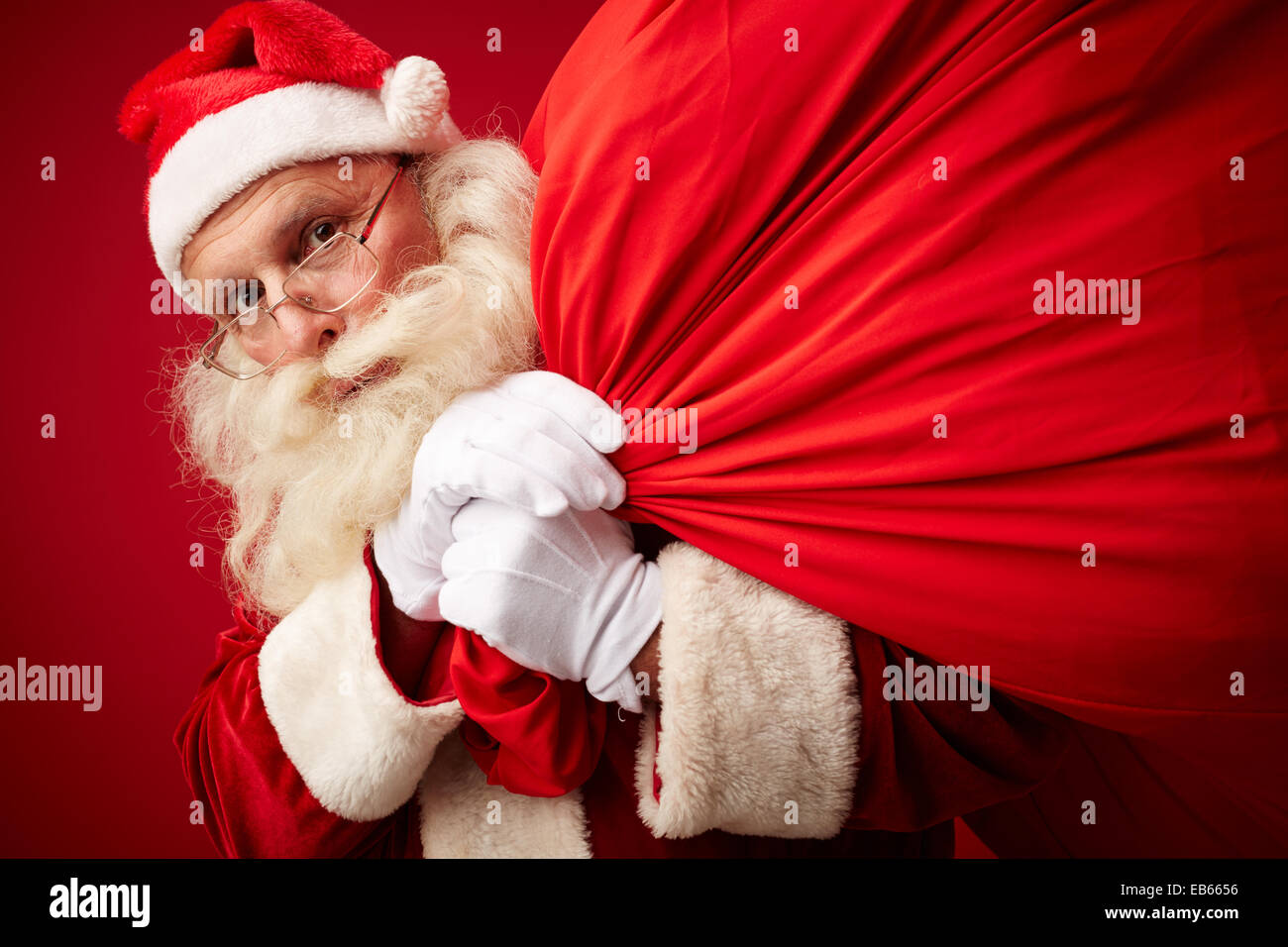 Portrait of Santa Claus with huge and heavy red sack looking at camera ...