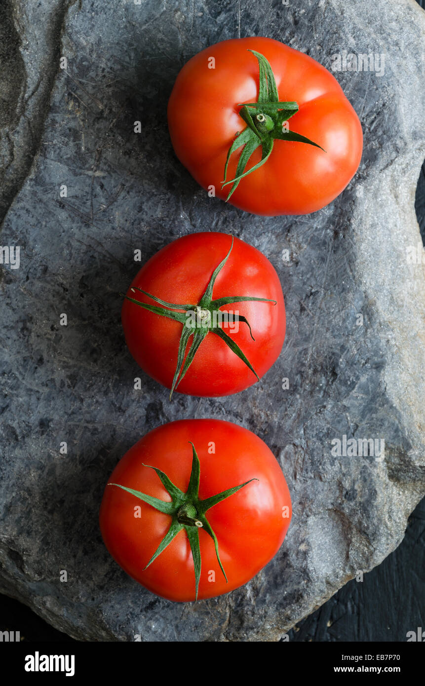 Three tomatoes over dark gray stone, above view Stock Photo - Alamy