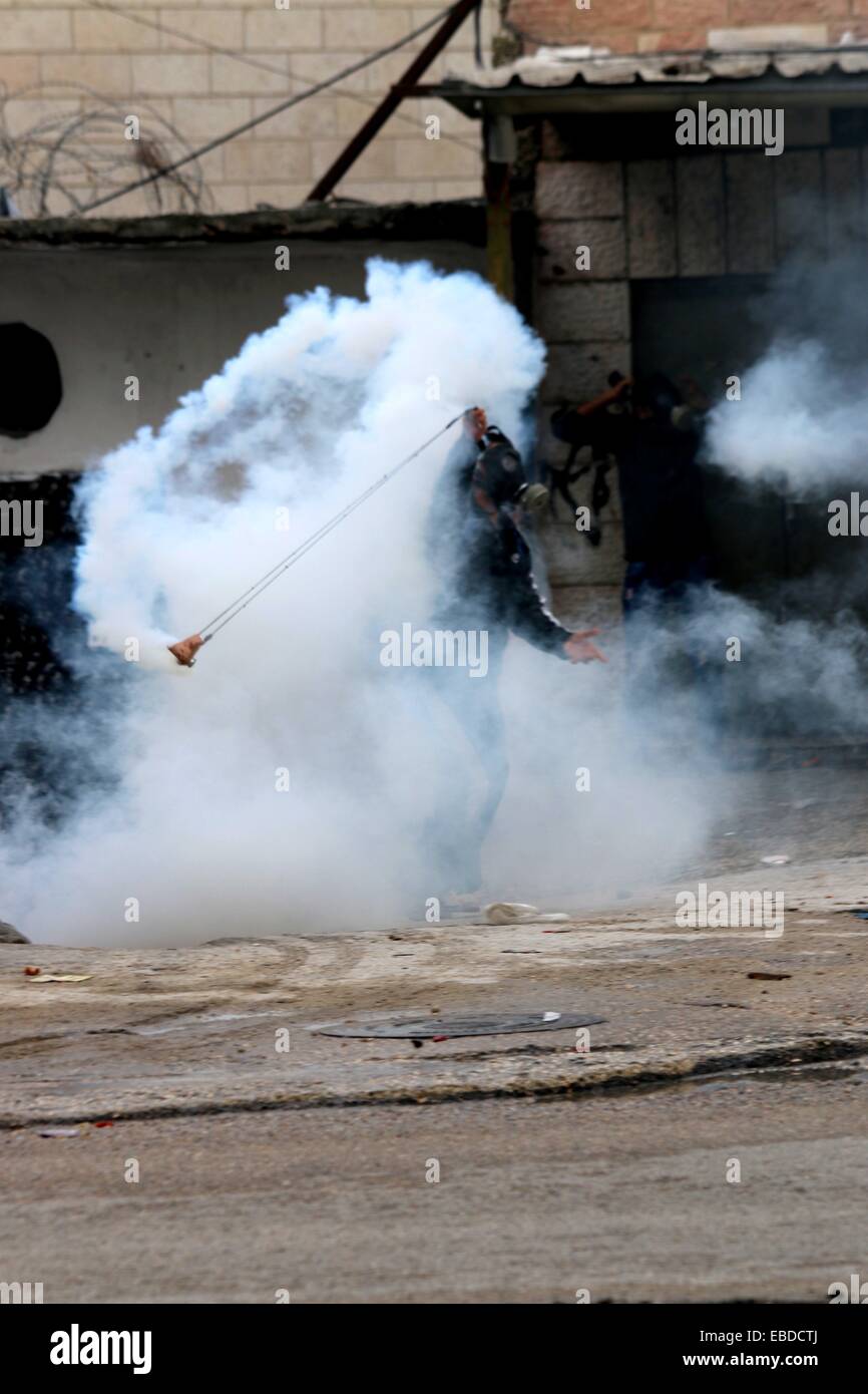 A Palestinian youth wearing a gas mask throws a tear gas canister back ...