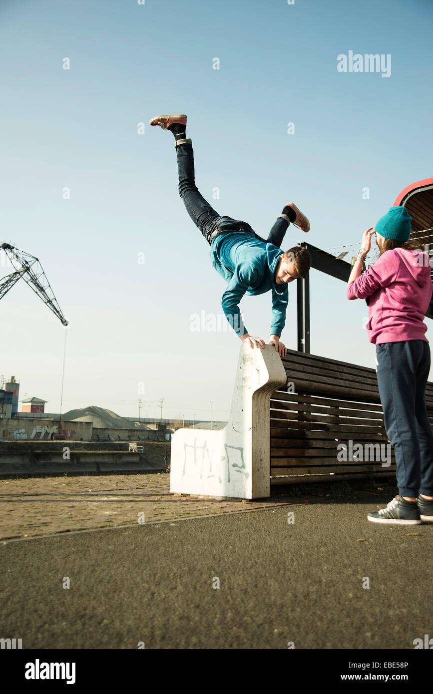 Teenage boy doing handstand on bench outdoors, while teenage girl ...