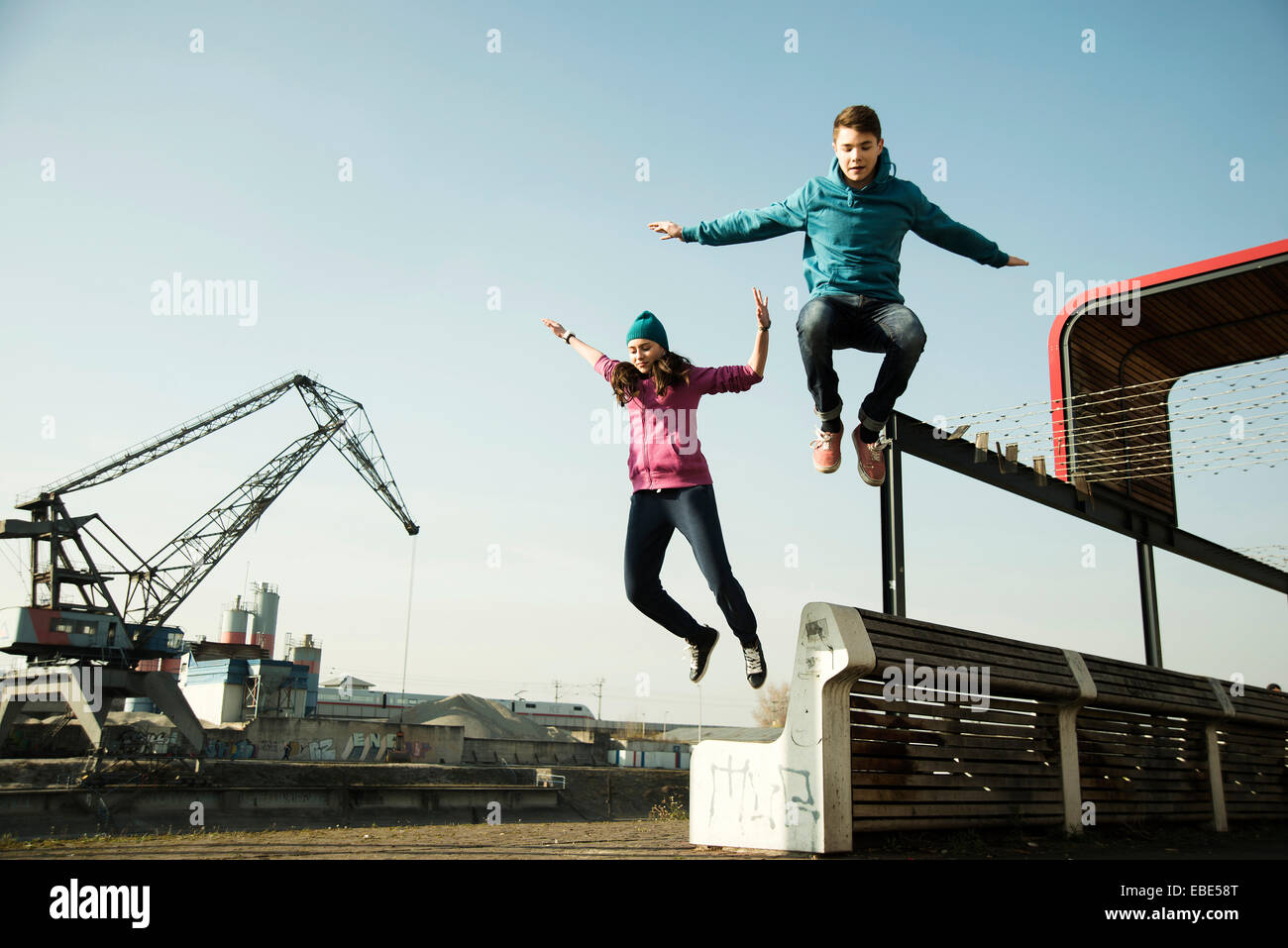 Teenage girl and boy jumping over bench outdoors, industrial area ...