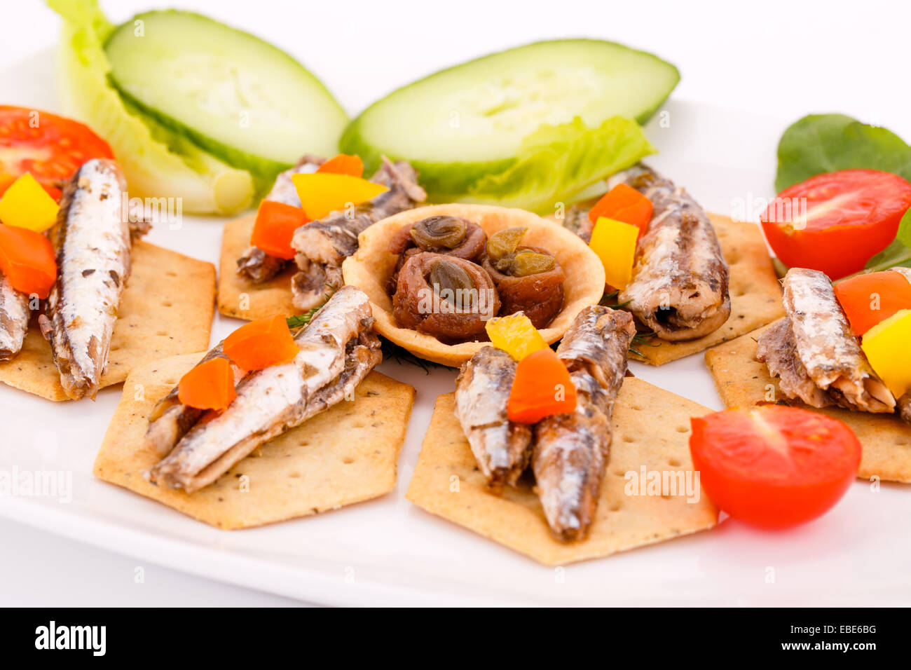 Fish and peppers on crackers with vegetables on white plate Stock Photo ...