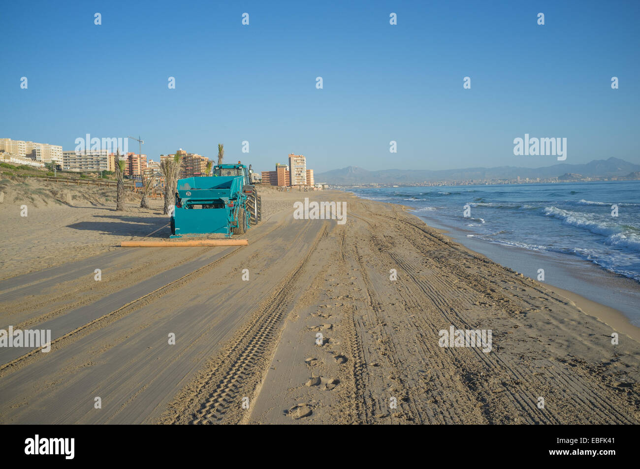 A tractor with a trailer cleaning a beach in the early hours of the ...