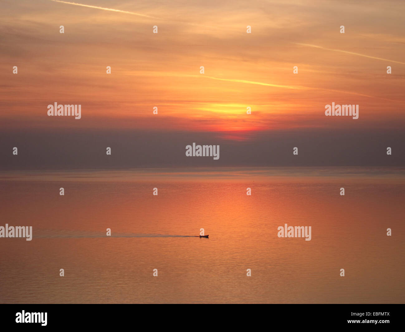 Beautiful red sunset over the ocean and little boat Stock Photo - Alamy
