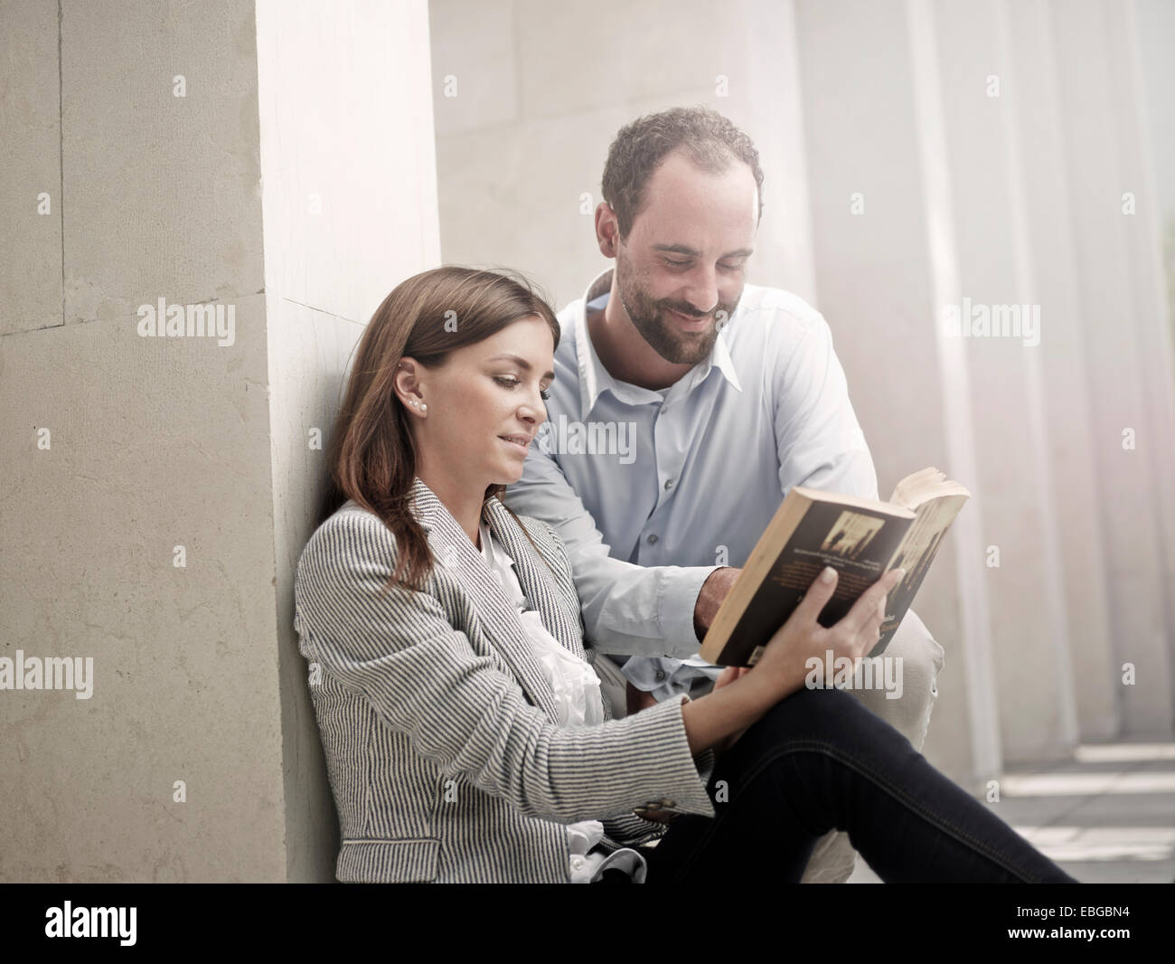 Woman leaning against a wall and reading a book, man looking curiously ...