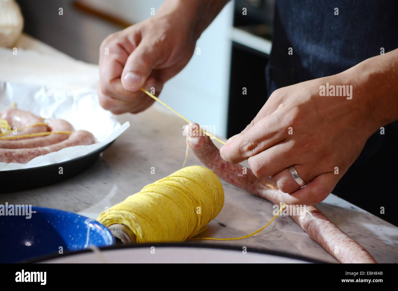 Chef's hands are tying up the end of the casing for a homemade pork ...