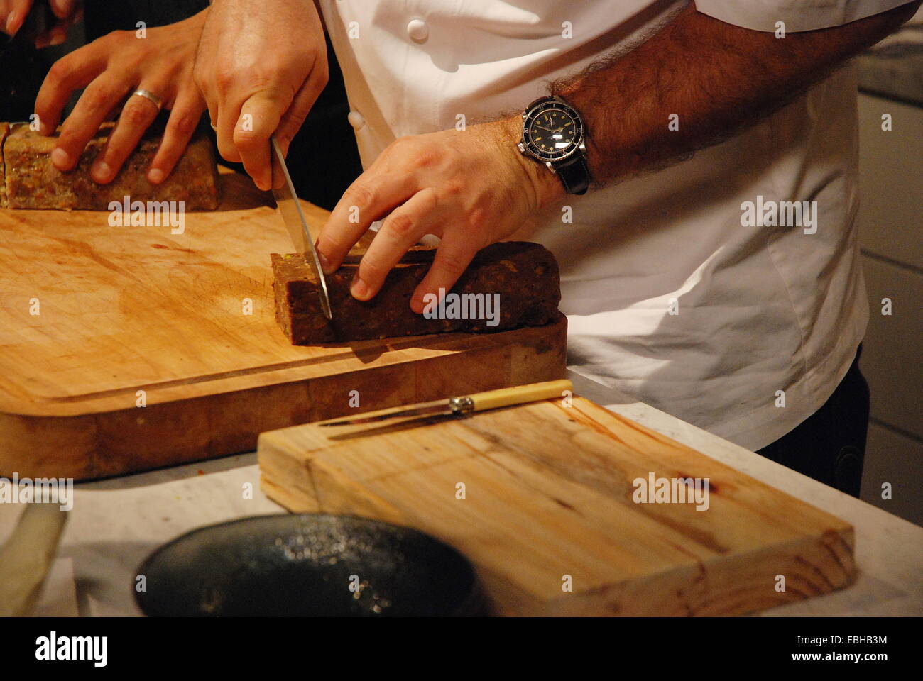 A chef is slicing a duck confit terrine on kitchen cutting board Stock ...