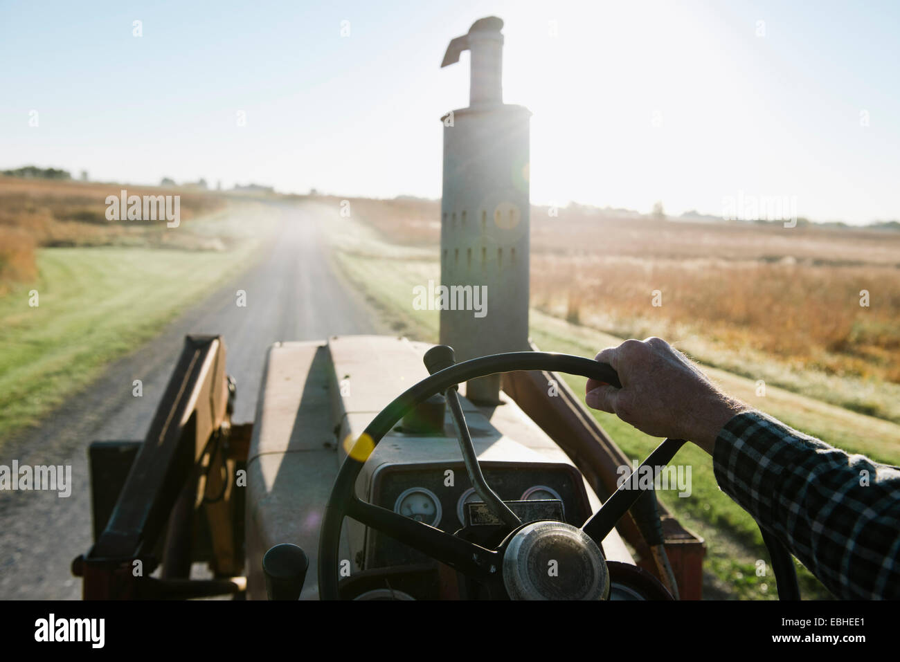 Over shoulder view of senior male farmer driving tractor on rural road ...