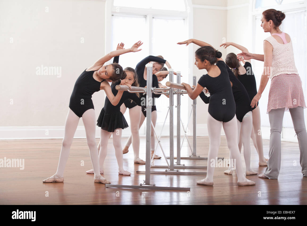 Ballet teacher teaching group of girls ballet position at the barre ...