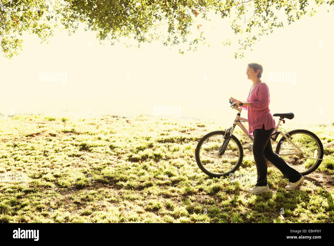 Mature woman pushing bicycle in park Stock Photo - Alamy