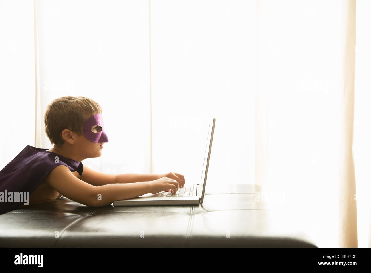 Boy in cape and mask using laptop at home Stock Photo - Alamy