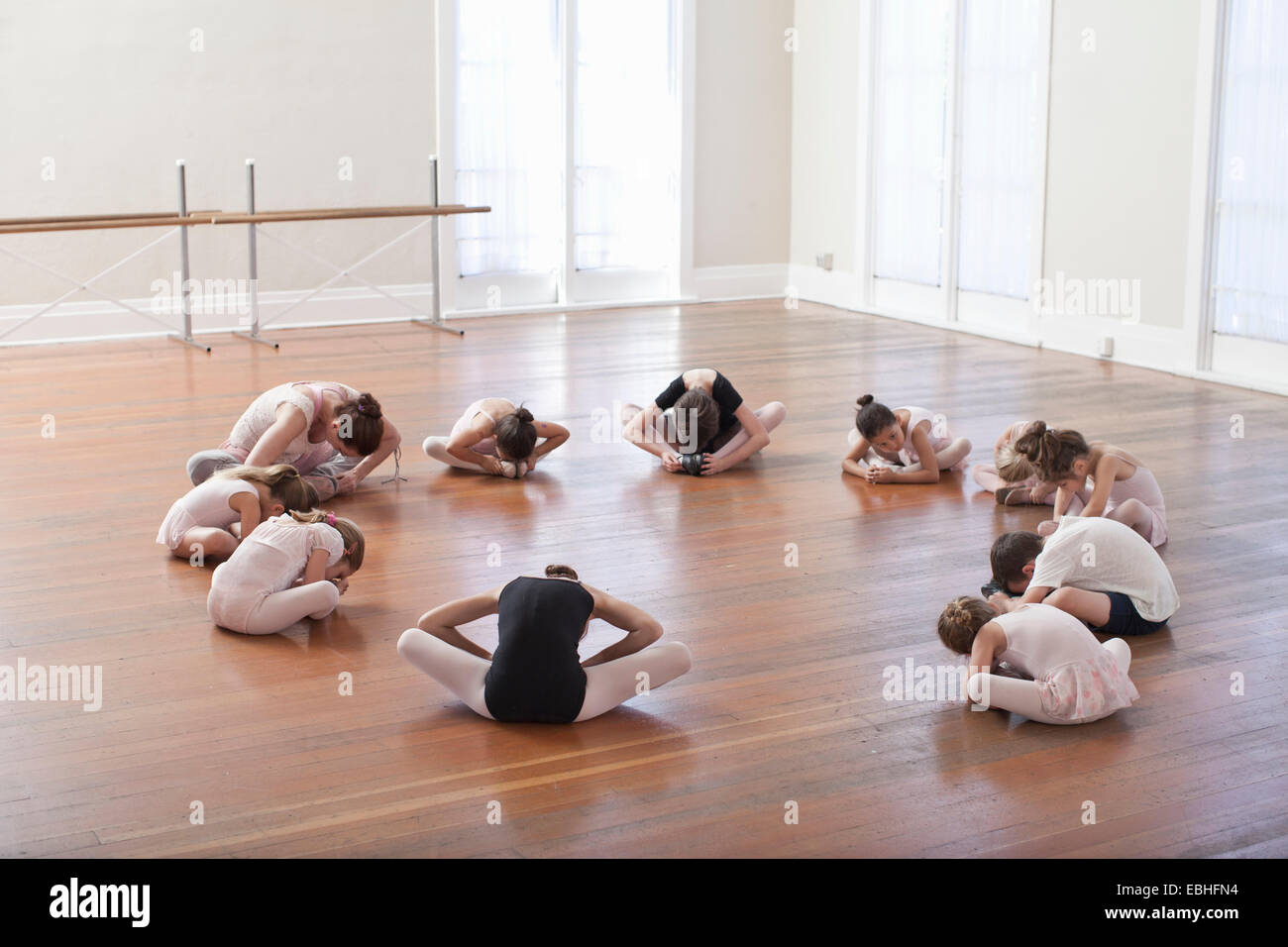Children sitting on floor practicing ballet with teacher in ballet ...