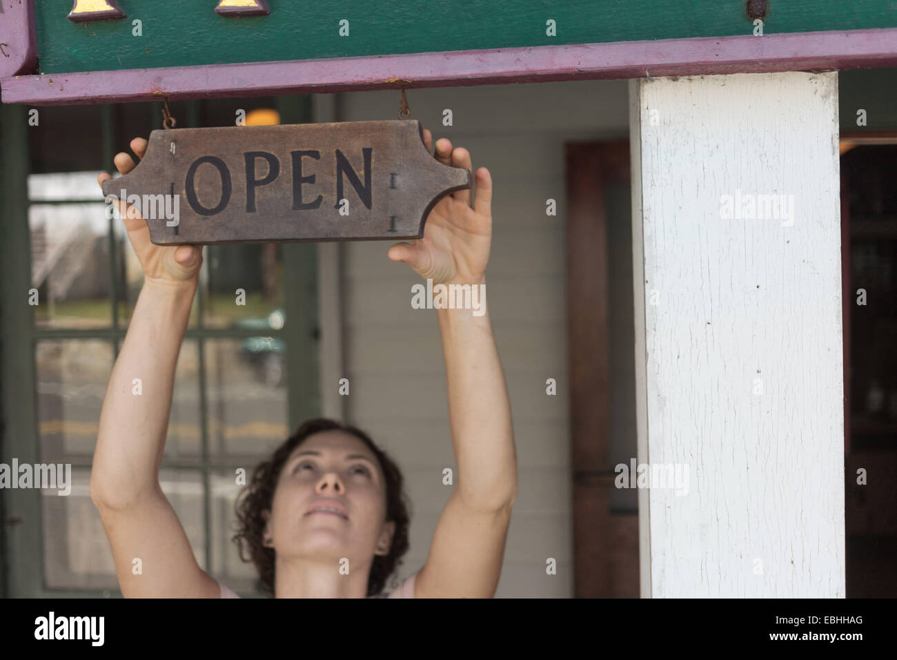 Female shop assistant reaching for open sign at country store Stock ...