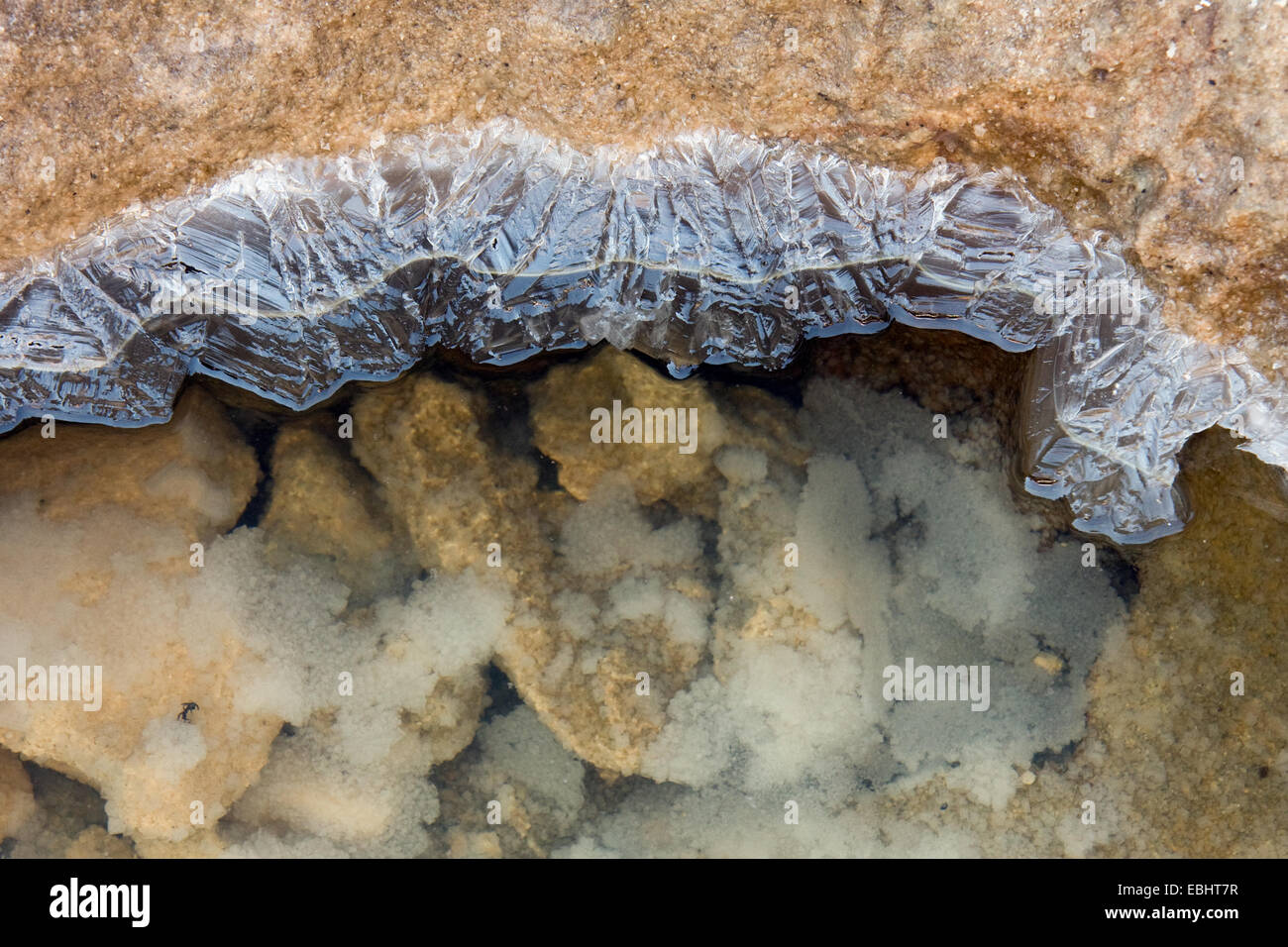 Salt crystals are forming in a small plash of water by the salt ...