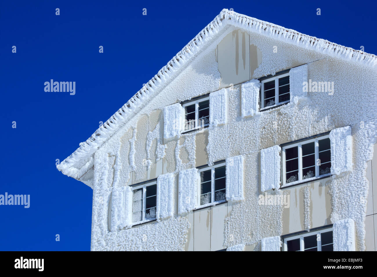 snow-covered facade of a residental house in front of a clear blue sky ...