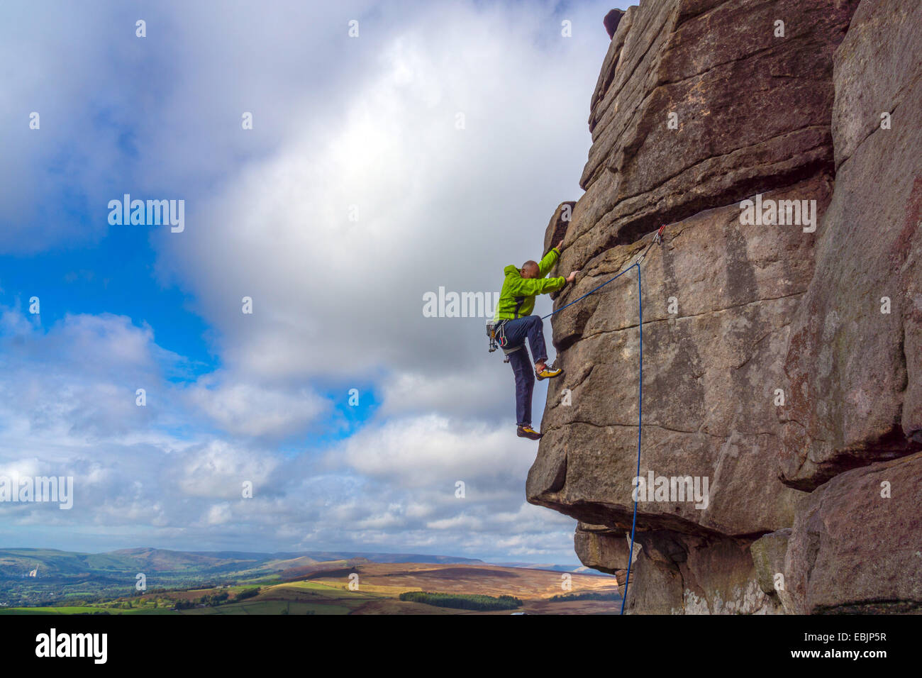 Rock climber on sheer cliff face, with panorama view at Stanage Edge ...