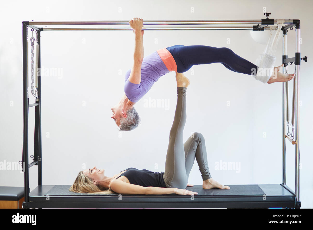 Two mature women practicing pilates on trapeze table in pilates gym ...