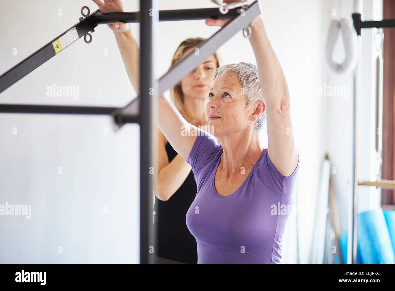 Female student and tutor practicing pilates on trapeze table in pilates ...