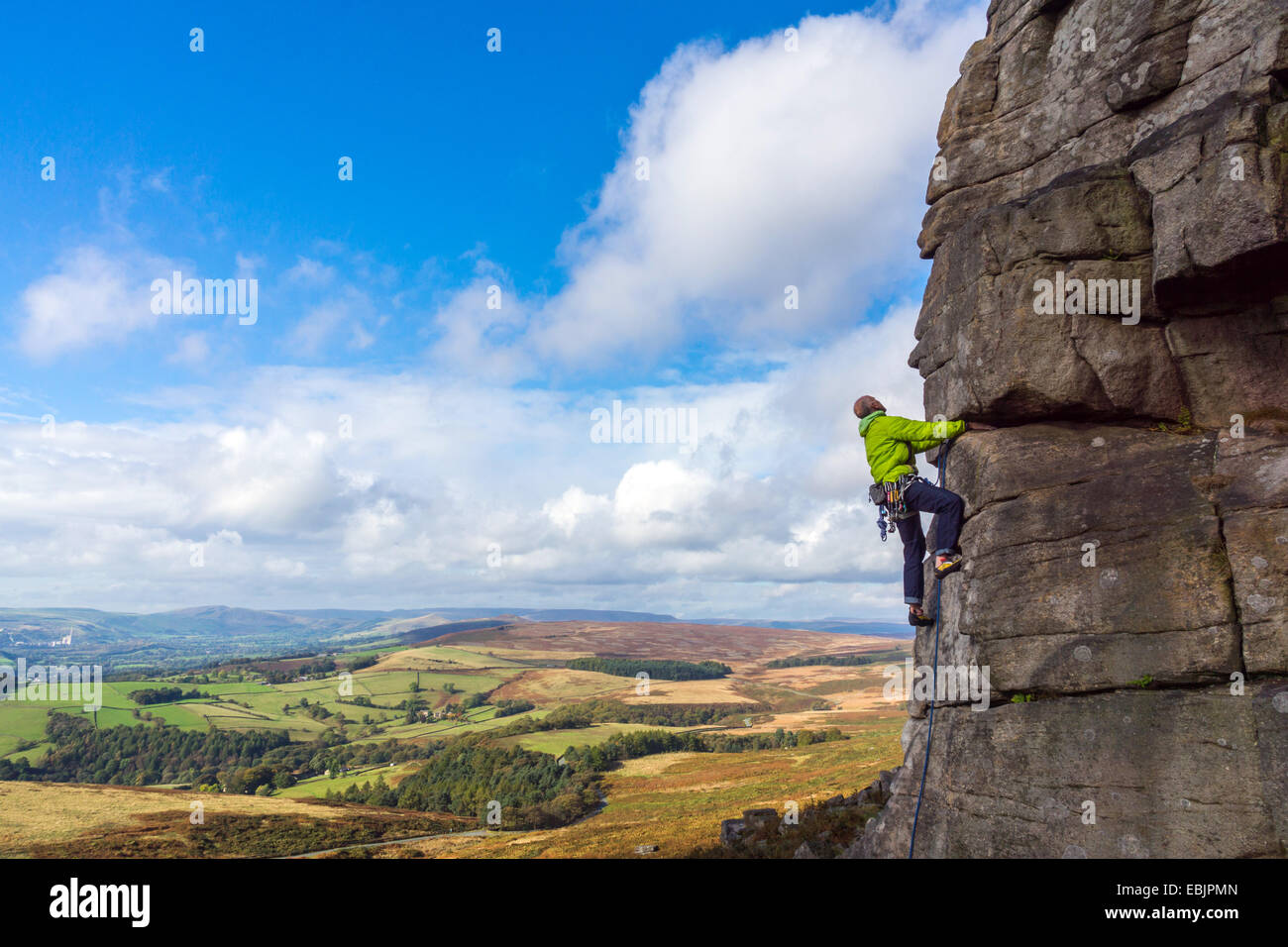 Rock climber on sheer cliff face, with panorama view at Stanage Edge ...