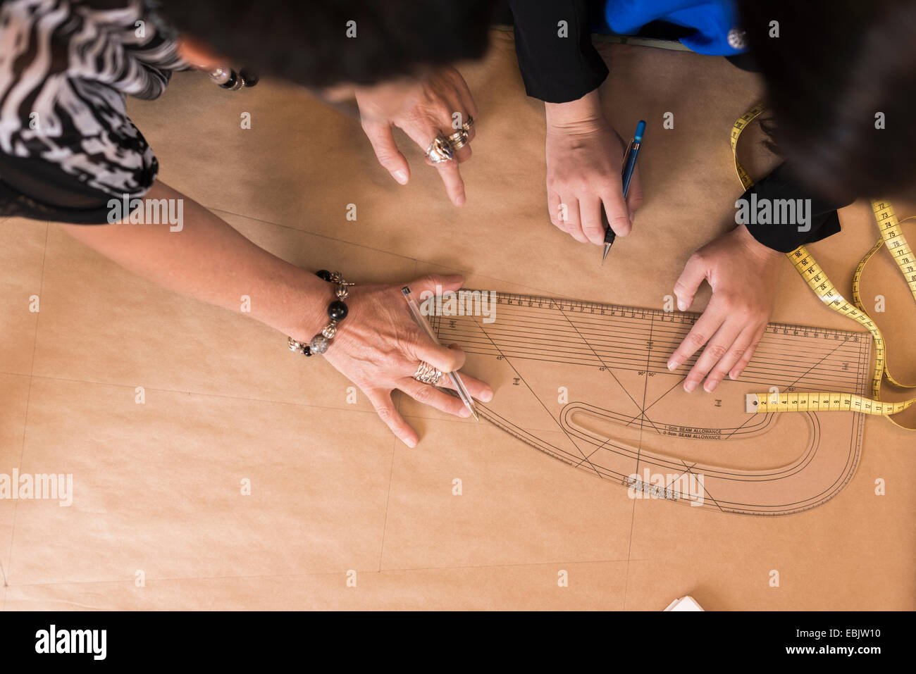 Overhead view of seamstresses hands using curved ruler on dressmakers ...