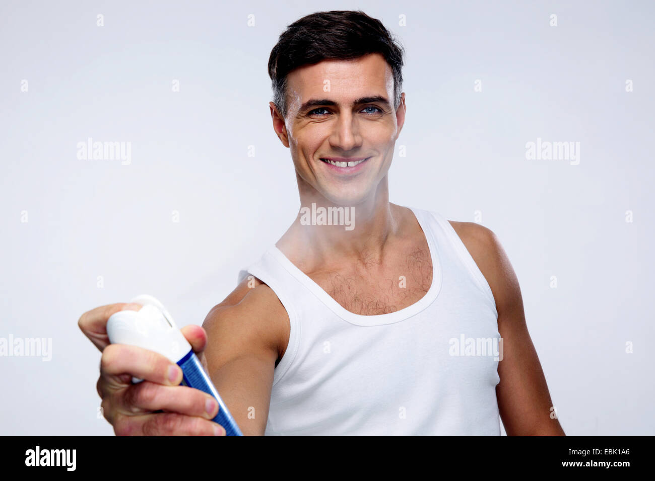 Happy man spraying deodorant over gray background Stock Photo - Alamy