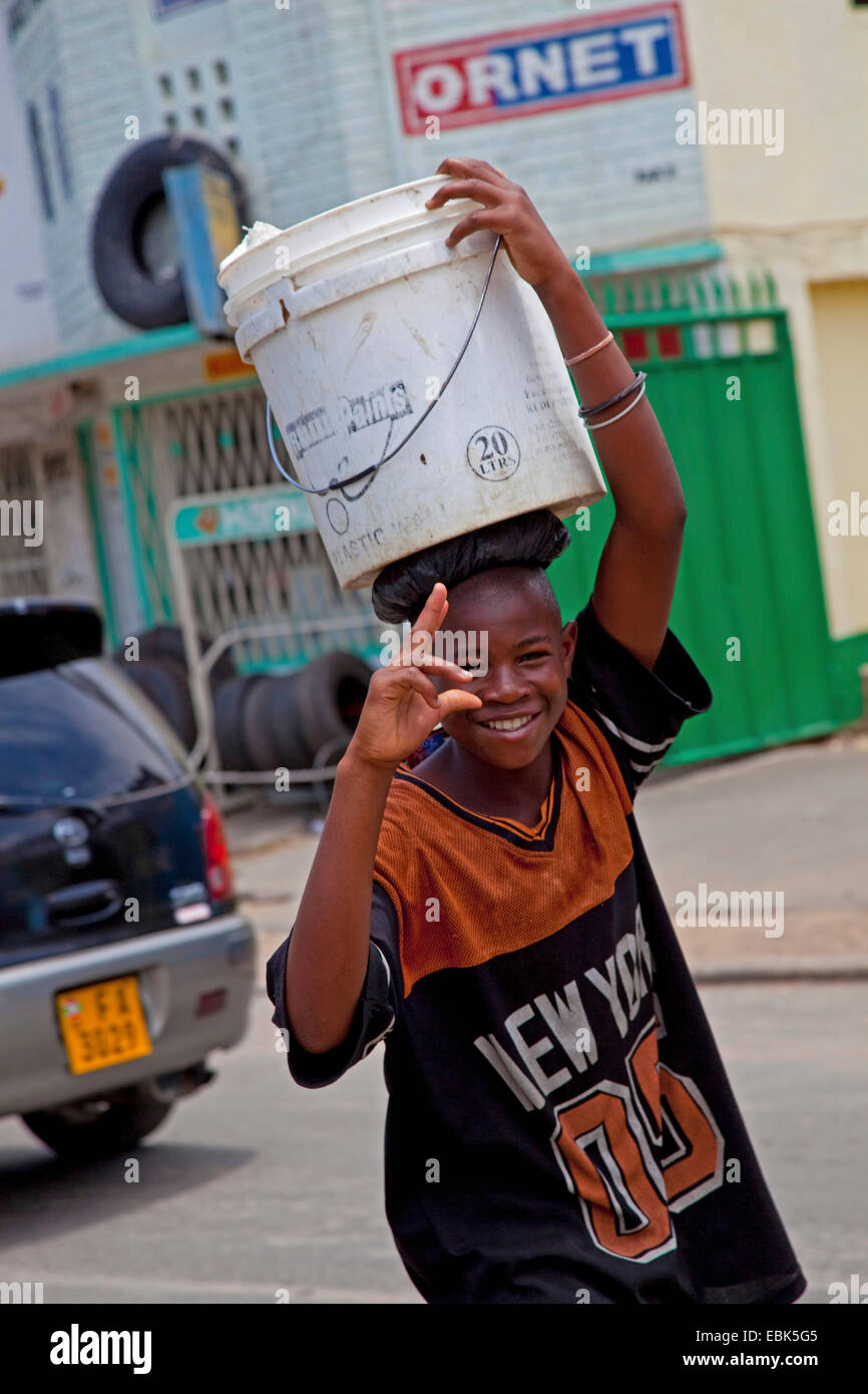 boy capping beaks while carrying a water bucket on his head through ...