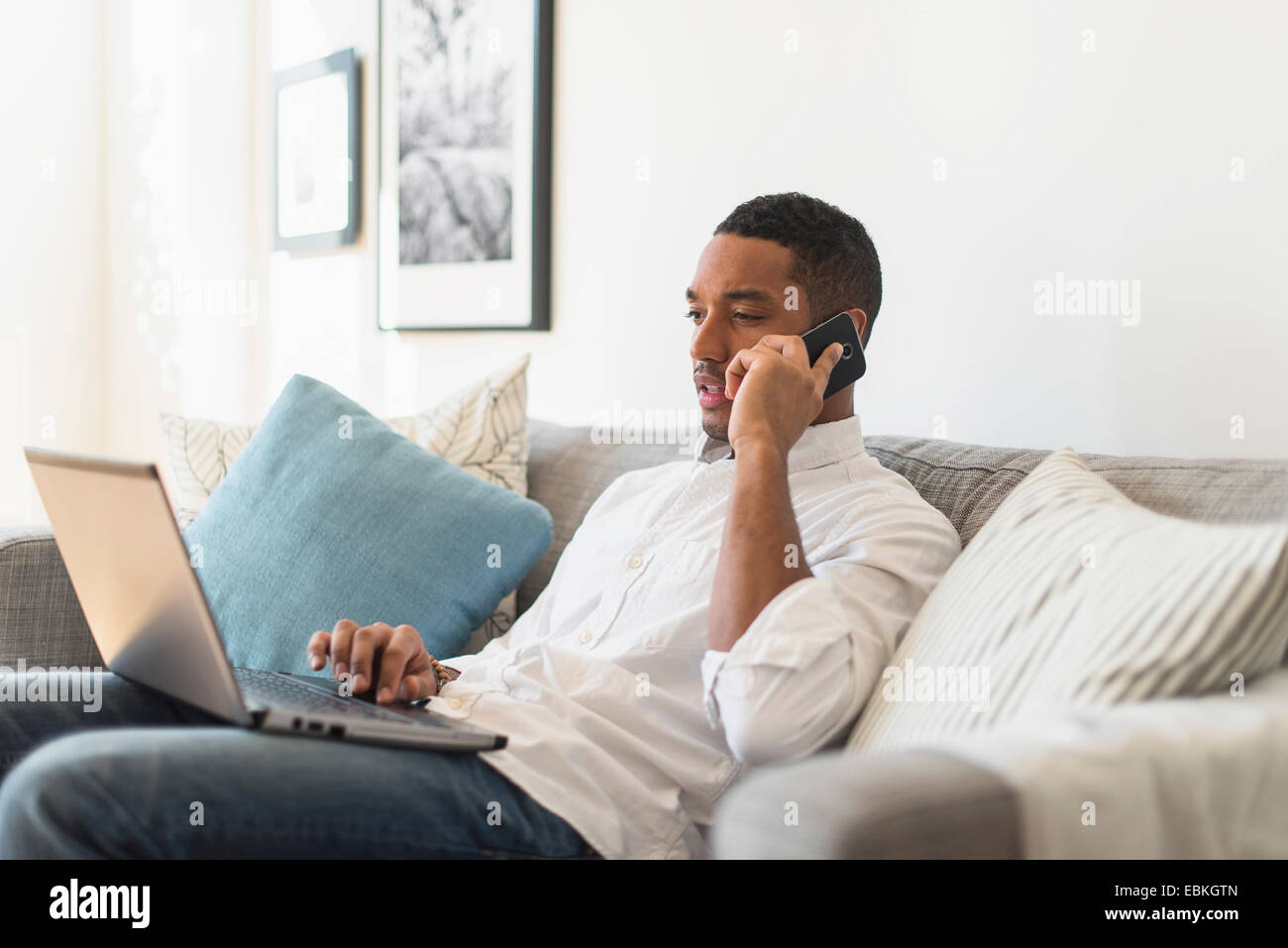 Man sitting in living room, using laptop and cell phone Stock Photo - Alamy