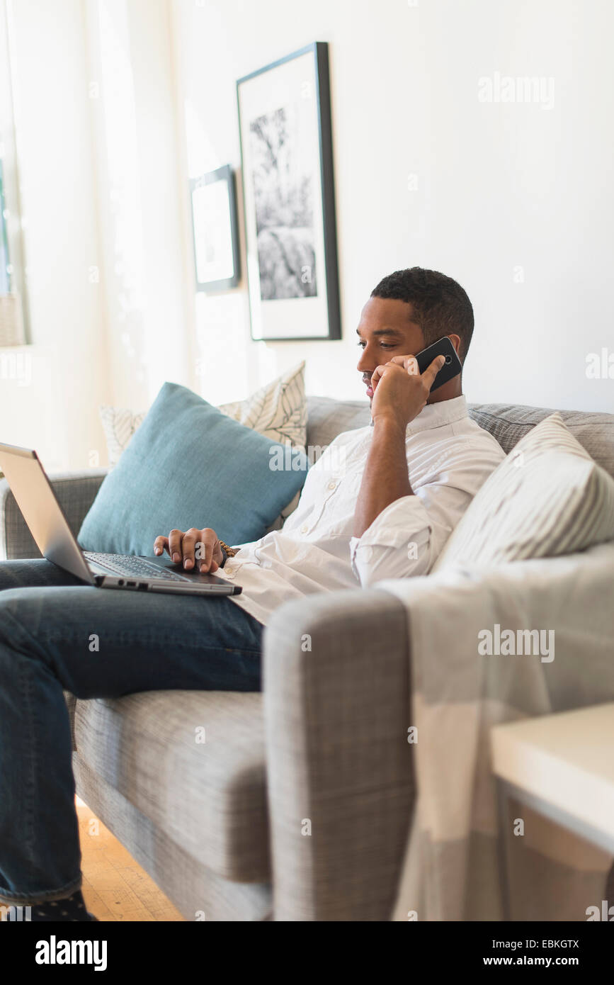 Man sitting in living room, using laptop and cell phone Stock Photo - Alamy