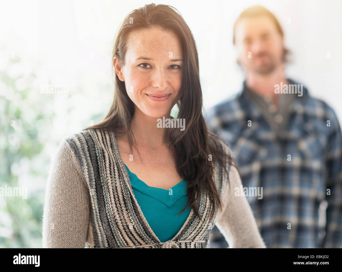 Smiling woman looking at camera, man in background Stock Photo - Alamy