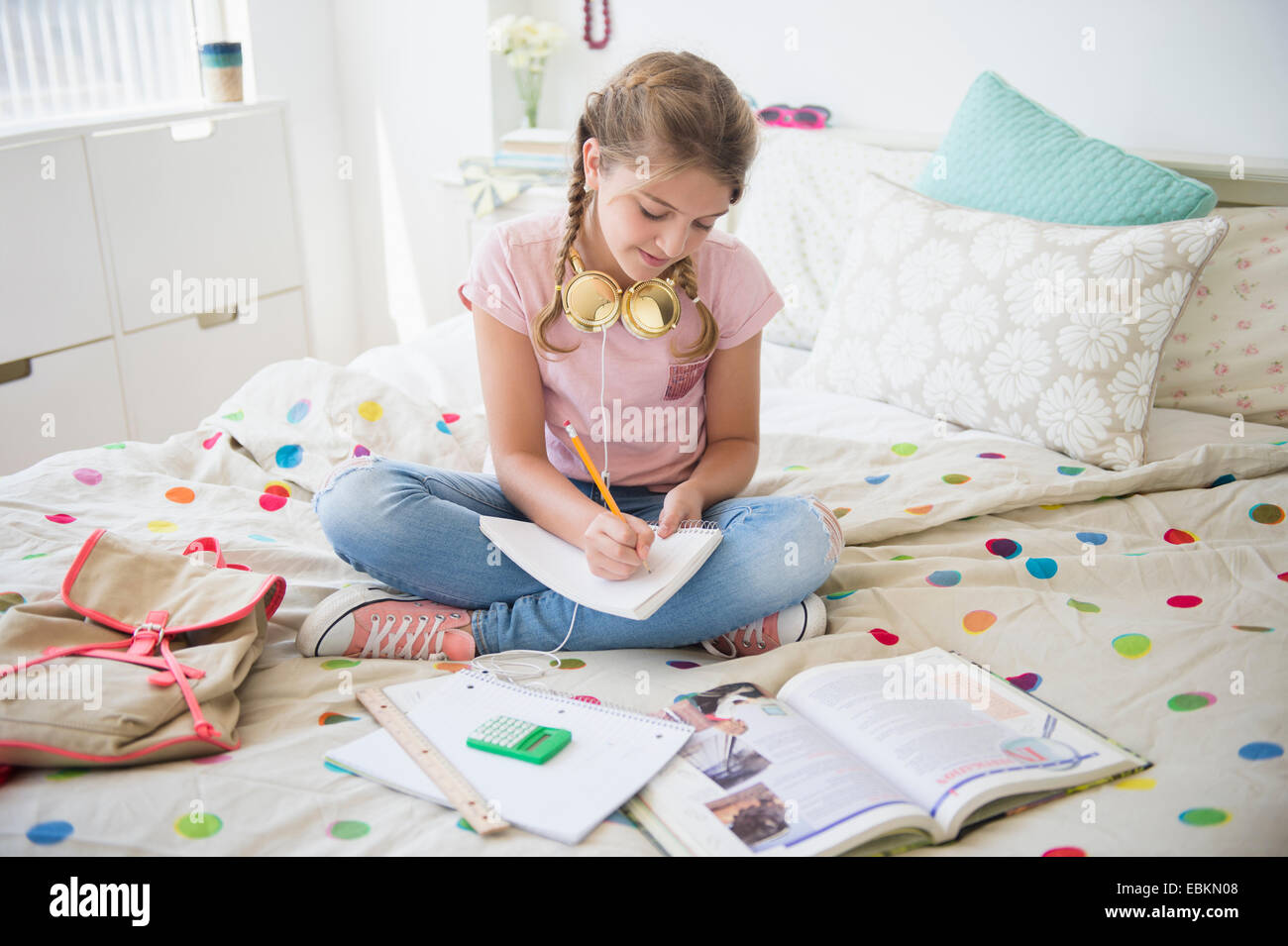 Girl (12-13) sitting on bed doing homework Stock Photo - Alamy