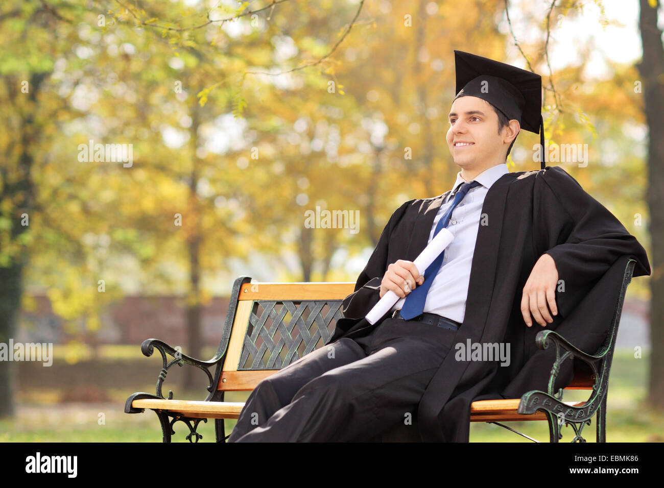 Graduate student holding diploma seated on bench in park Stock Photo ...