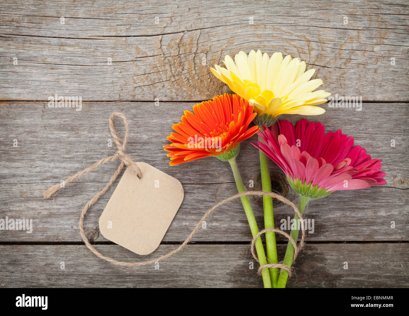 Three colorful gerbera flowers with tag on wooden table Stock Photo - Alamy