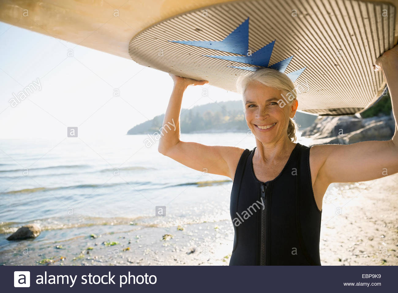 Senior woman holding paddle board overhead on beach Stock Photo - Alamy