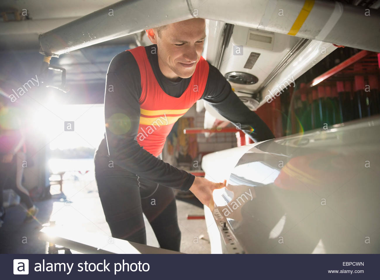 Rower lifting scull from rack in boathouse Stock Photo - Alamy