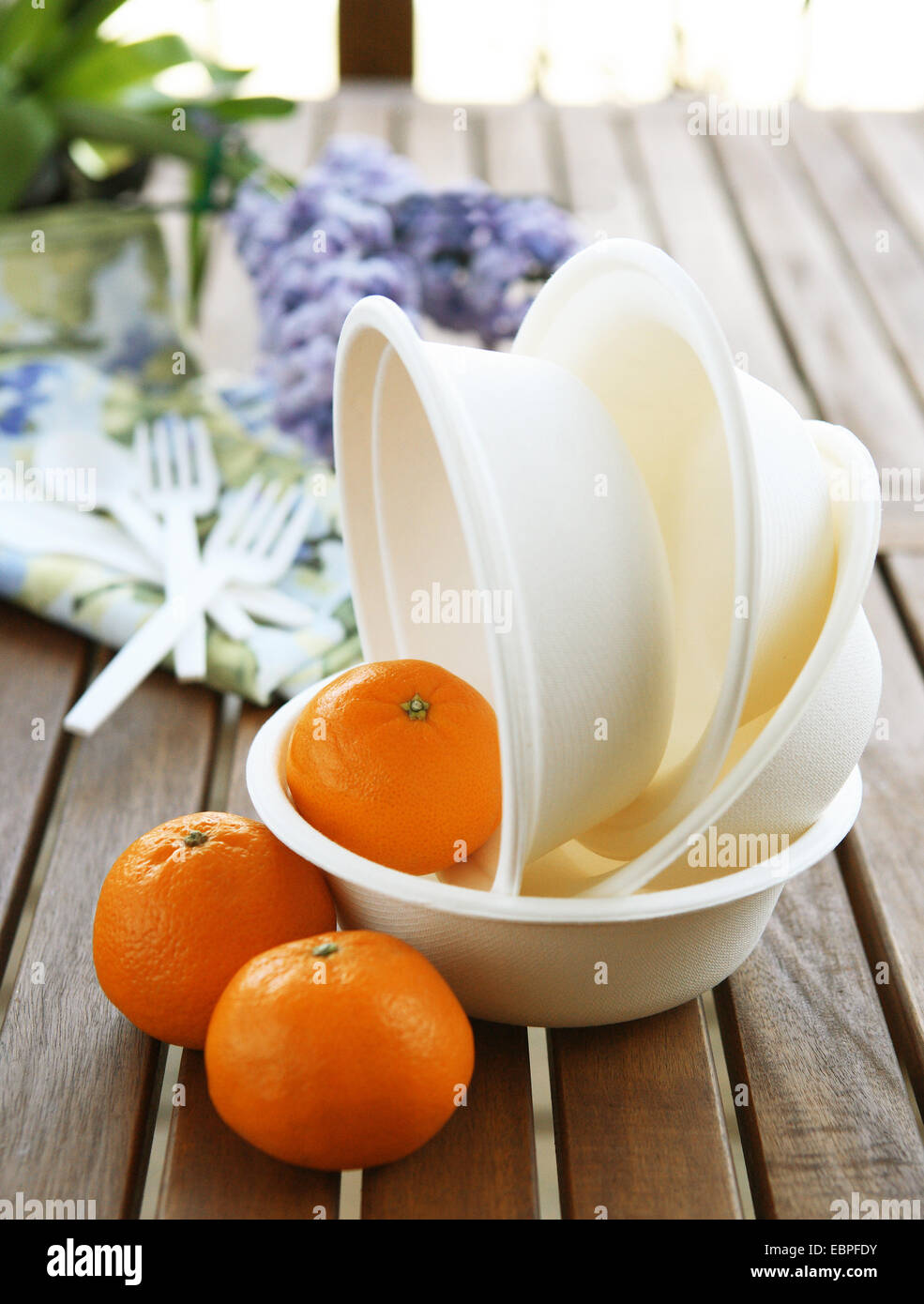 stacked paper bowls with tangerines on a wood table with flowers in the ...