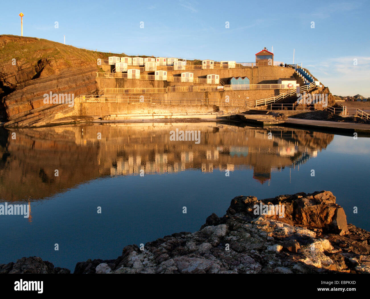 Beach huts reflected in the water of the Bude sea pool, Cornwall, UK ...